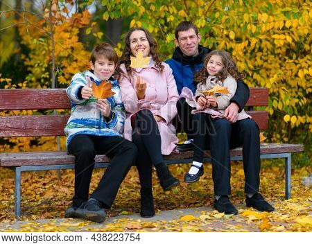 Portrait of a happy family in an autumn park. People sitting on a bench ...