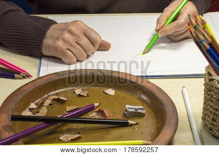 A person draws on a paper with colored pencils, with the left hand ...
